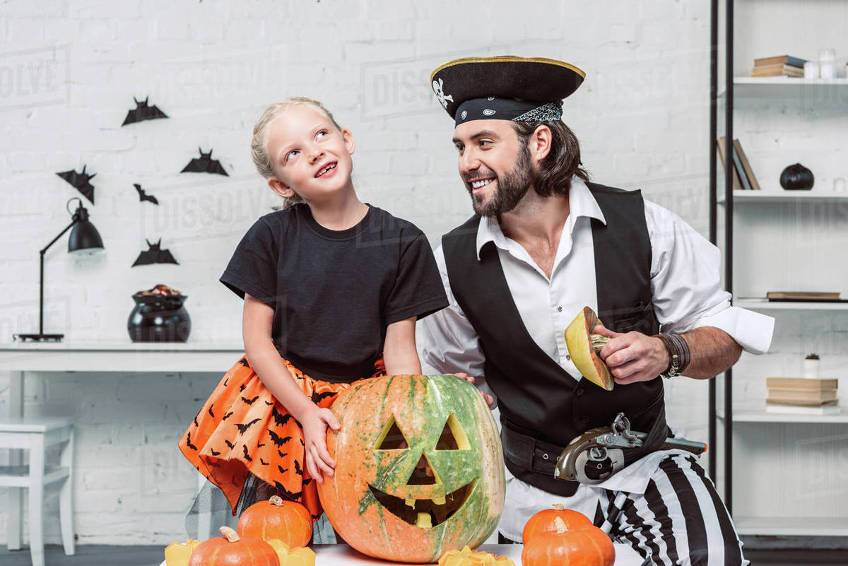 Smiling father and daughter in halloween costumes at table with pumpkin ...