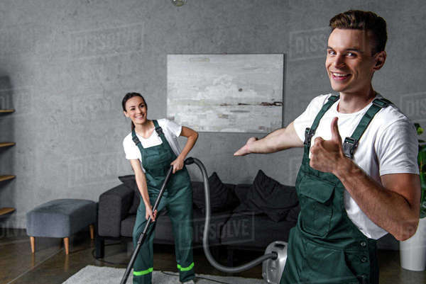 Smiling young man showing thumb up and showing beautiful female cleaner ...