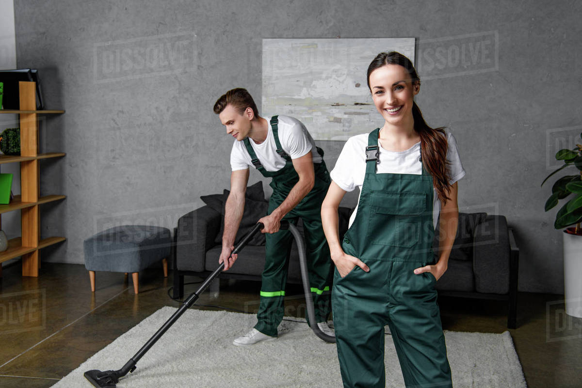 Young cleaning company workers using vacuum cleaner and smiling at ...