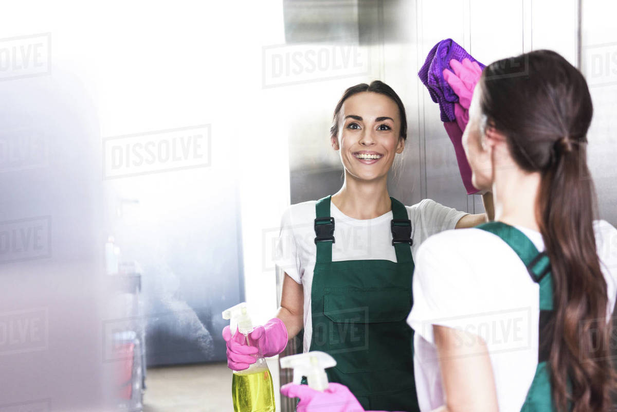 Smiling young female cleaner washing elevator with rag and detergent ...