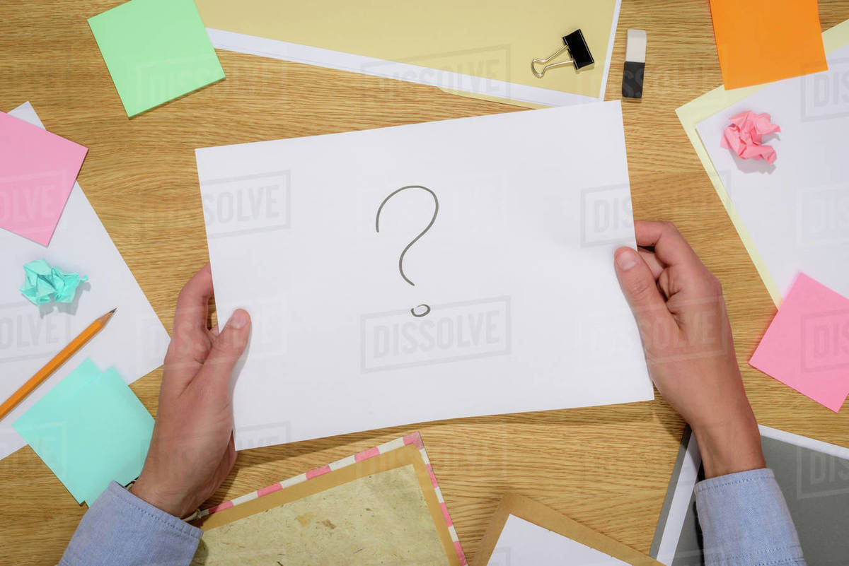 Cropped image of woman holding paper with question mark over table with ...