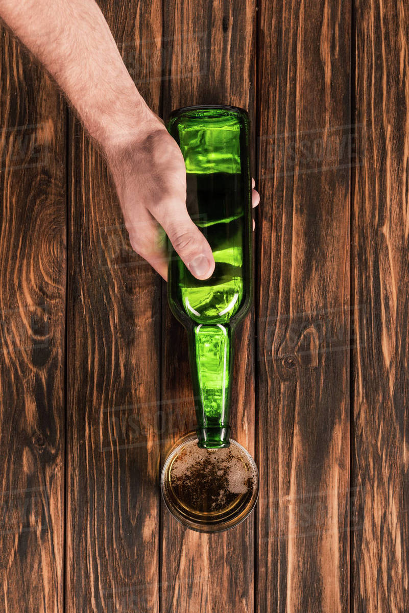 Partial view of man pouring beer into glass at wooden table - Stock ...