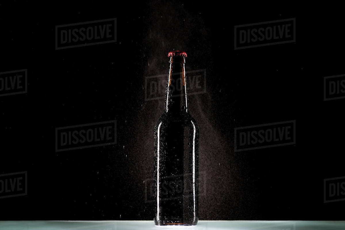 Bottle of beer with spraying water at table on black background ...