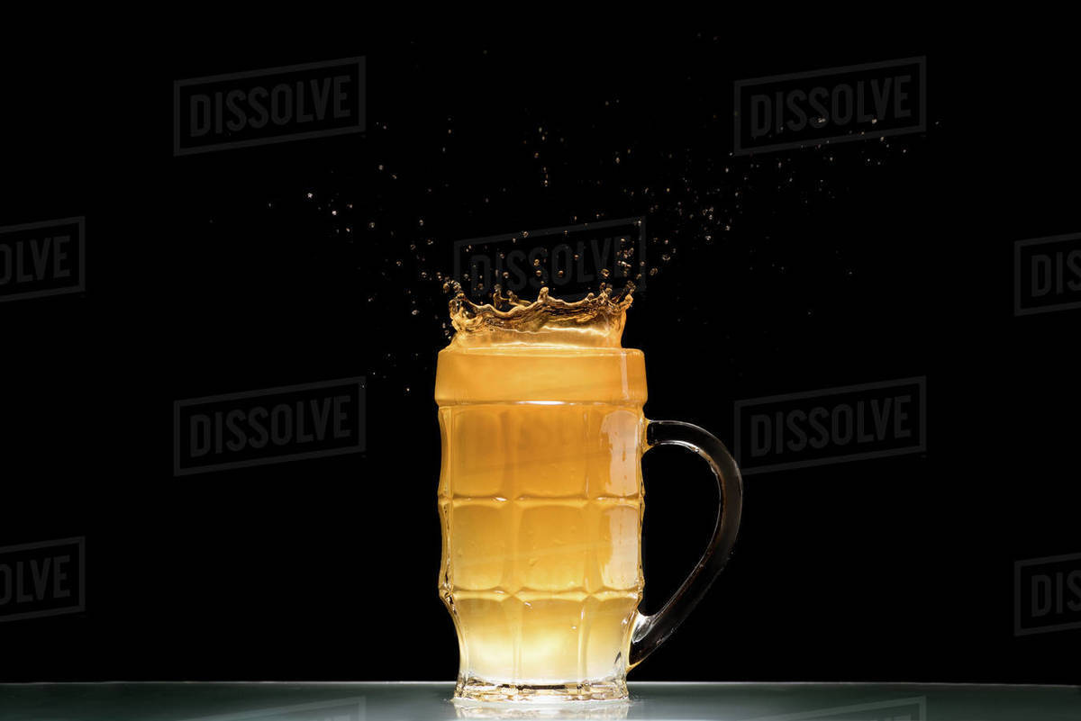 Glass of light beer with splashes at table on black background ...