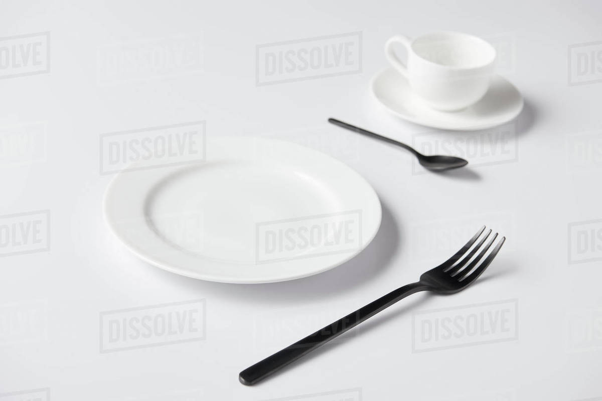 Selective focus of plate, fork, spoon and cup on white table - Royalty ...