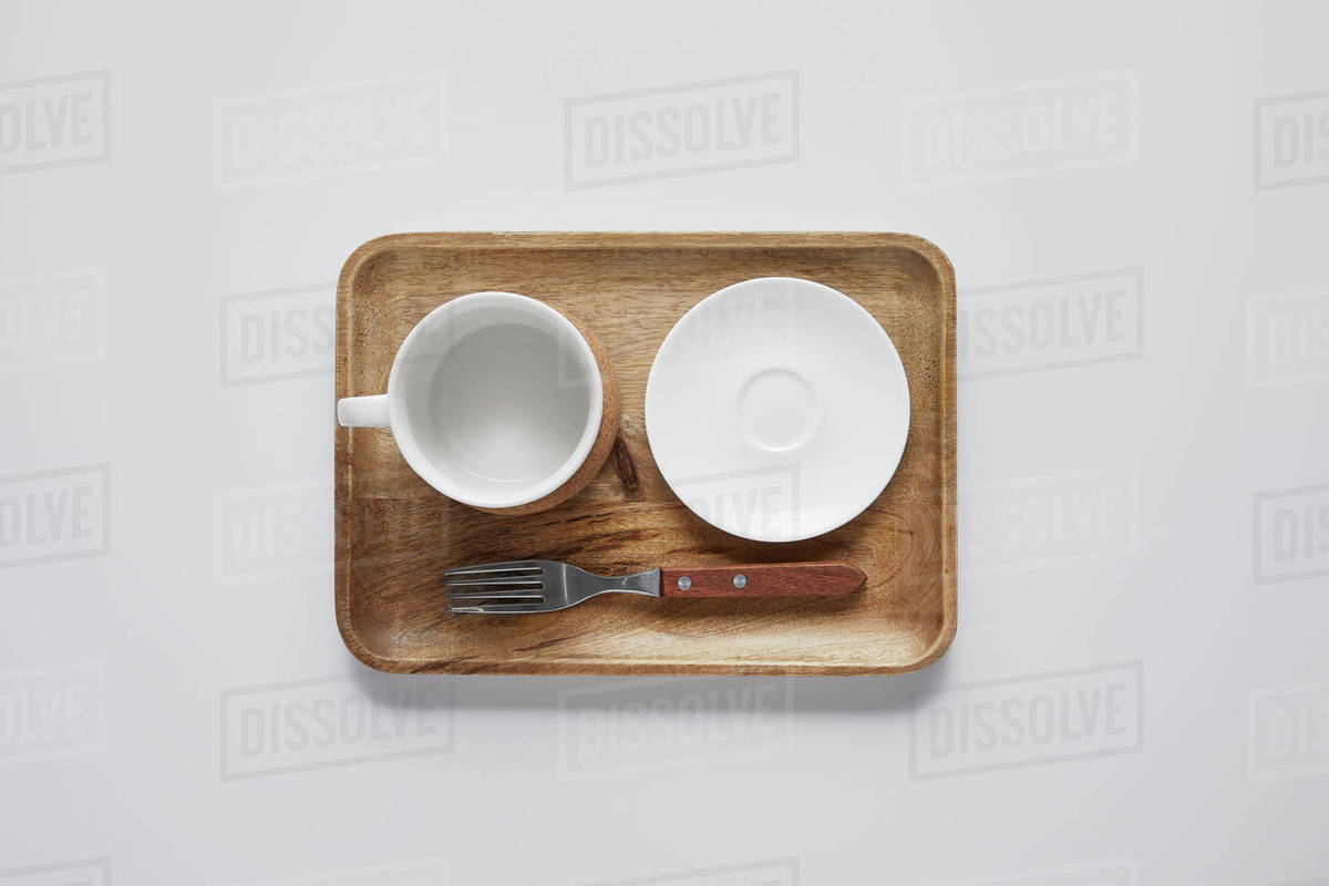 Top view of wooden tray with plate, bowl and fork on white table ...