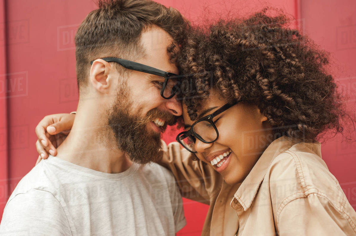 Happy young multicultural couple in eyeglasses hugging on street ...