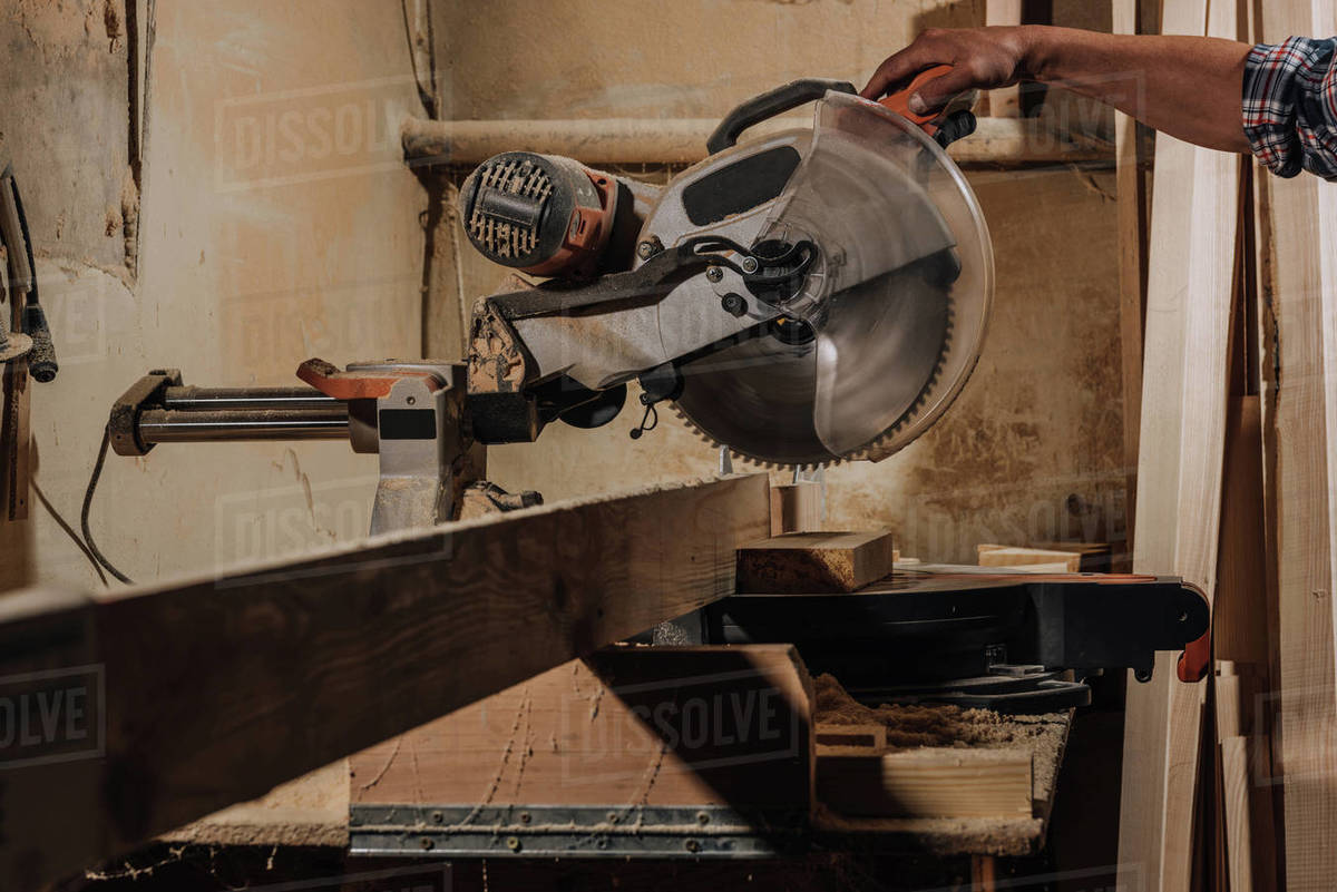 Partial view of carpenter using circular saw at wooden workshop ...