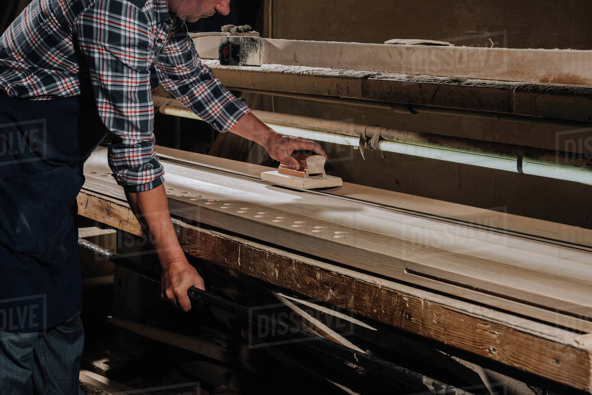 Cropped shot of woodworker planning wood with hand plane at workshop ...
