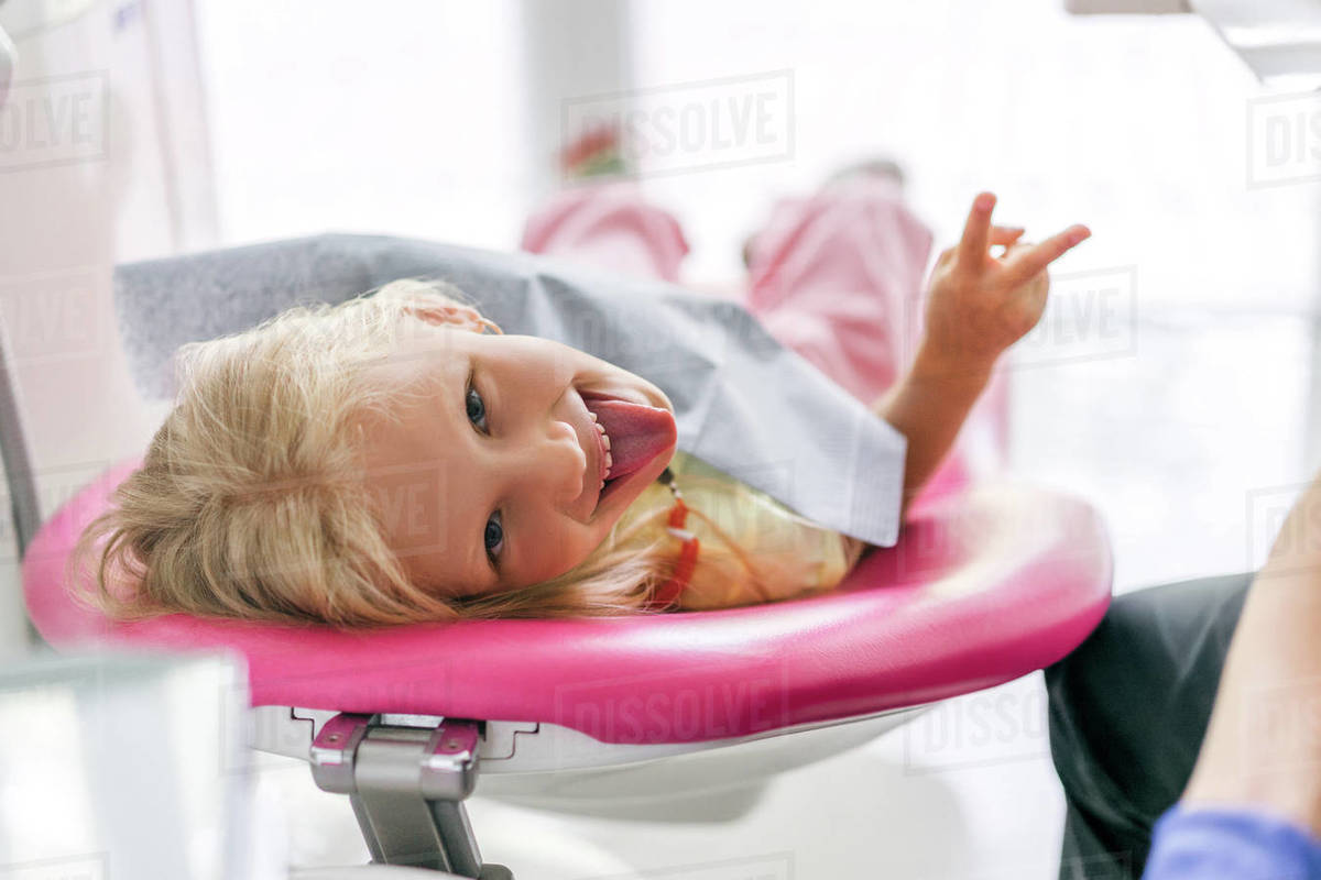 Portrait of child sticking tongue out and showing peace sign at dentist ...