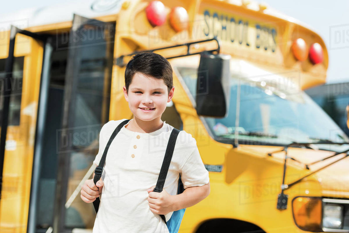 smiling little schoolboy with backpack standing in front of school bus ...