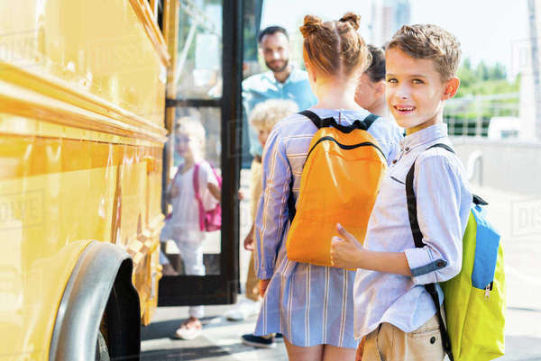 smiling little schoolboy entering school bus with classmates while ...