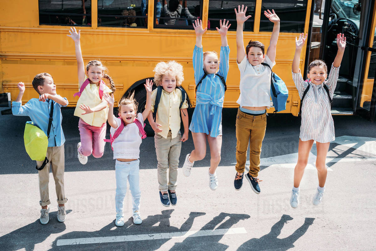 group of adorable schoolchildren jumping in front of school bus and ...