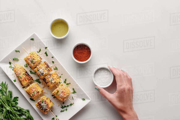 Cropped image of woman taking salt from marble table with grilled corn ...