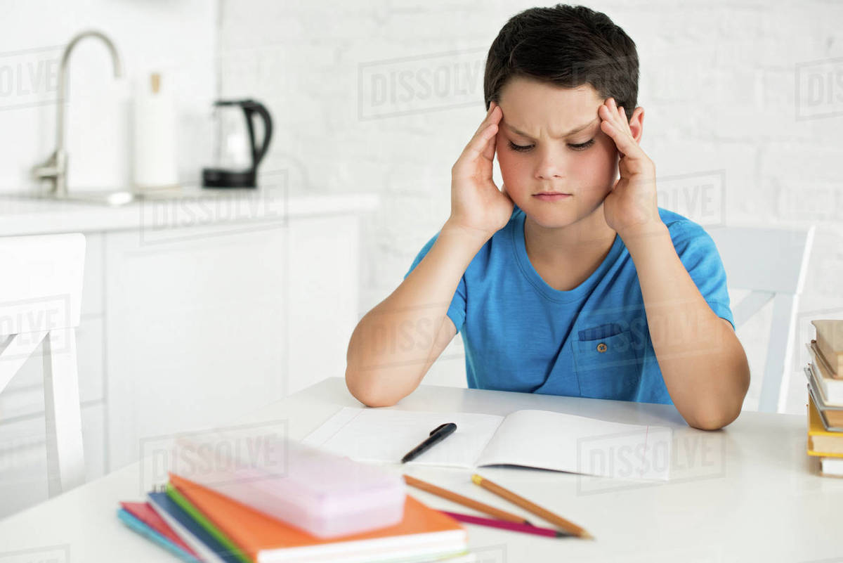 portrait of focused boy sitting at table with copybook, pen and ...