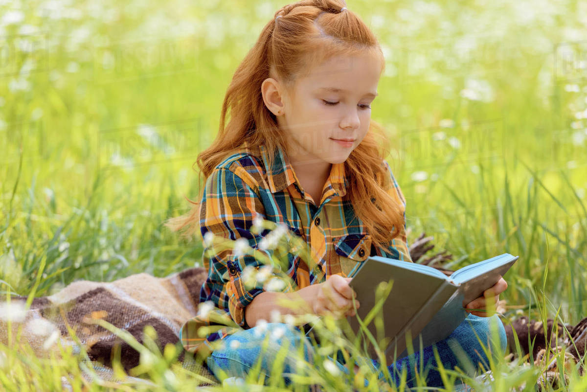 portrait of adorable red hair child reading book while sitting in ...