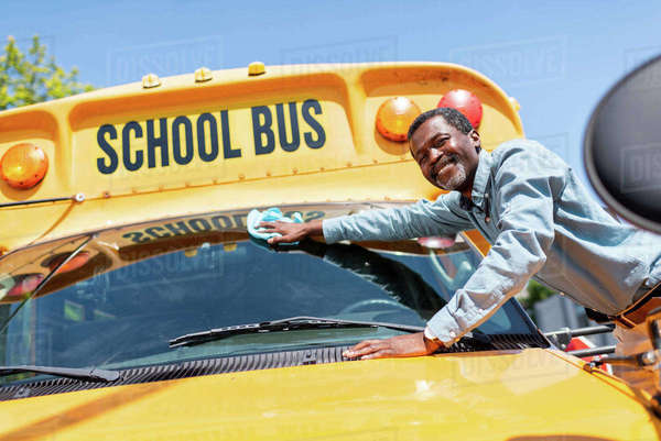 smiling mature african american bus driver wiping front window of ...