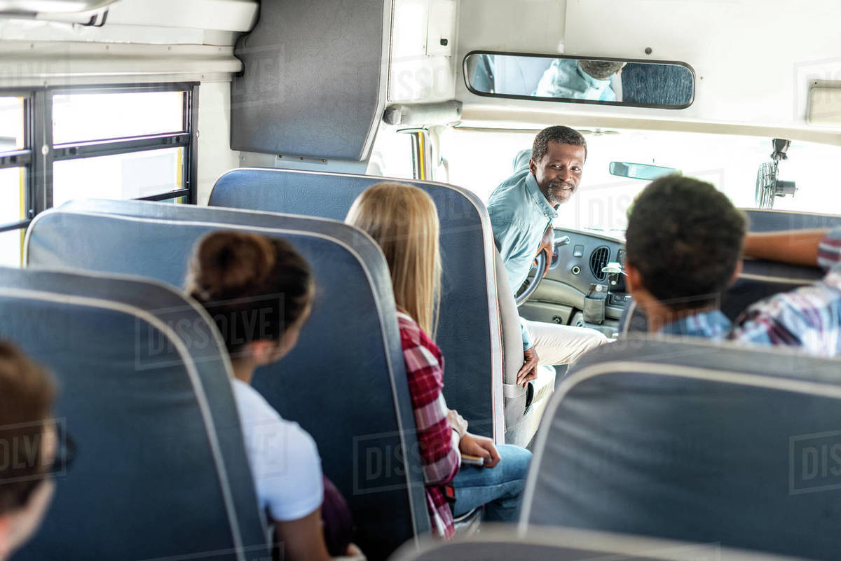 group of teen scholars riding school bus and talking with happy mature ...