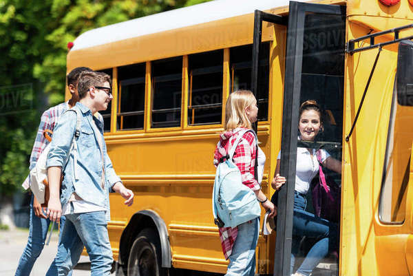group of happy teen scholars entering school bus after lessons ...