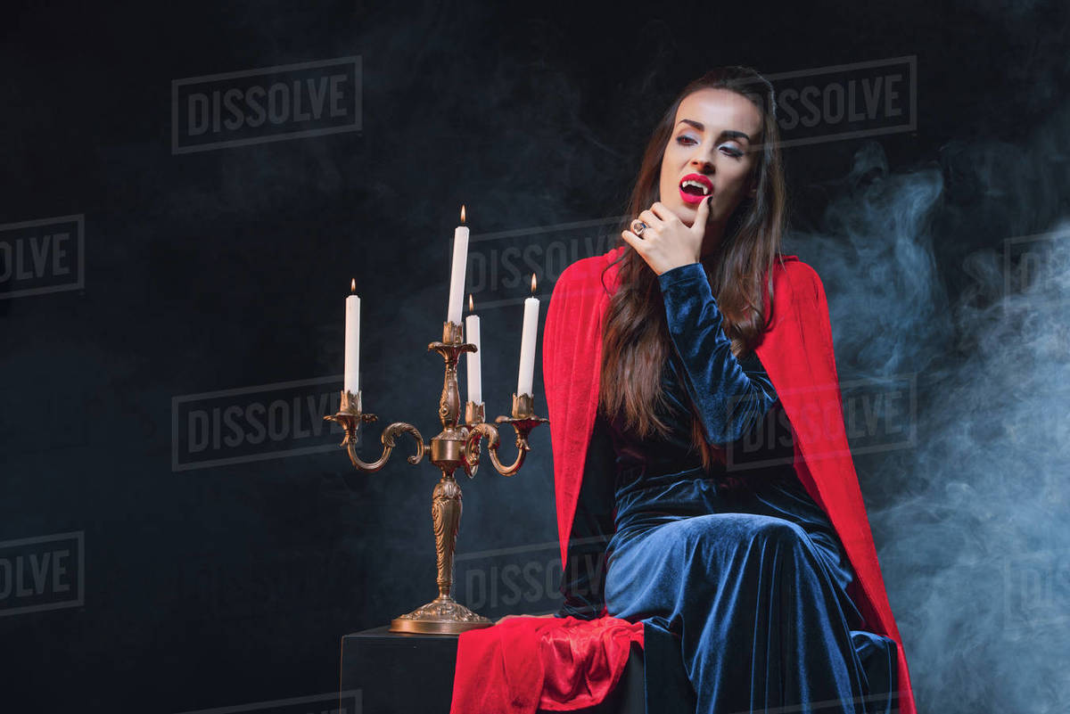 Beautiful woman in vampire costume sitting near candelabrum and licking ...