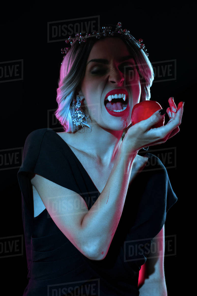 Vampire biting red bloody apple isolated on black - Stock Photo - Dissolve