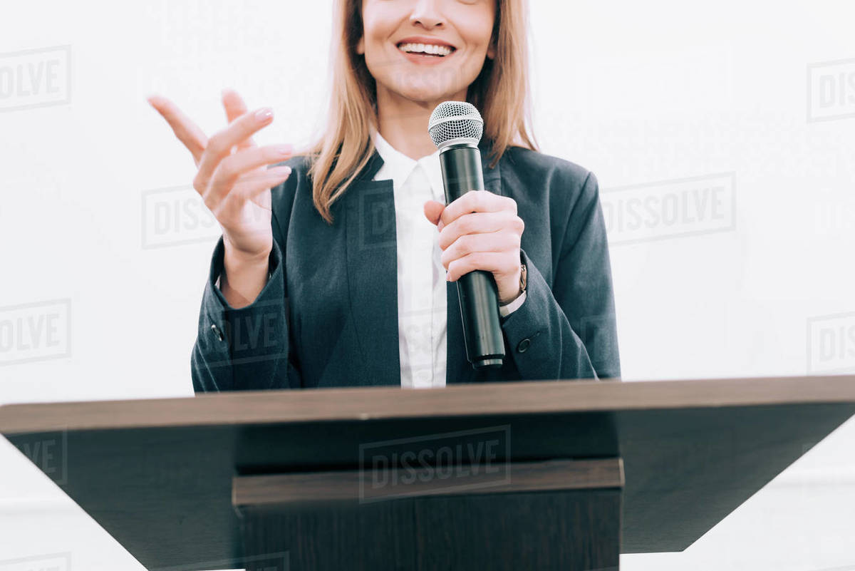 Cropped image of smiling speaker gesturing and talking at podium ...
