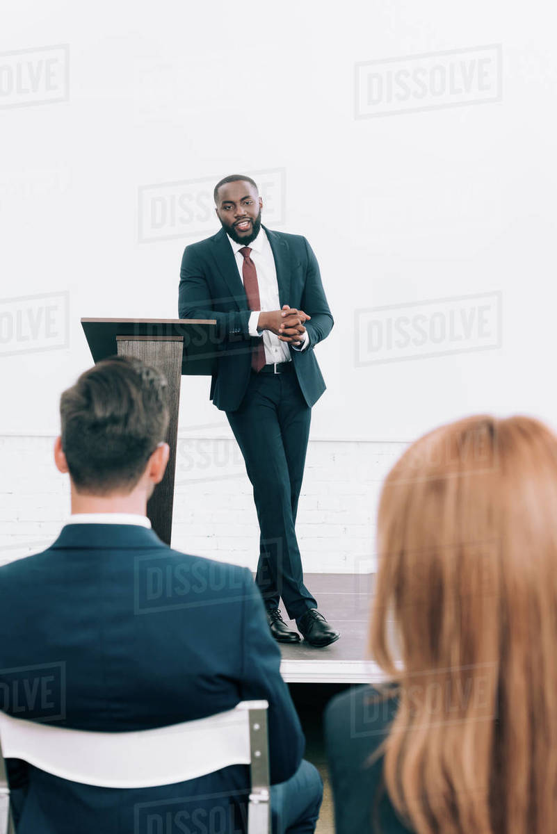 Handsome african American speaker leaning on podium tribune during ...