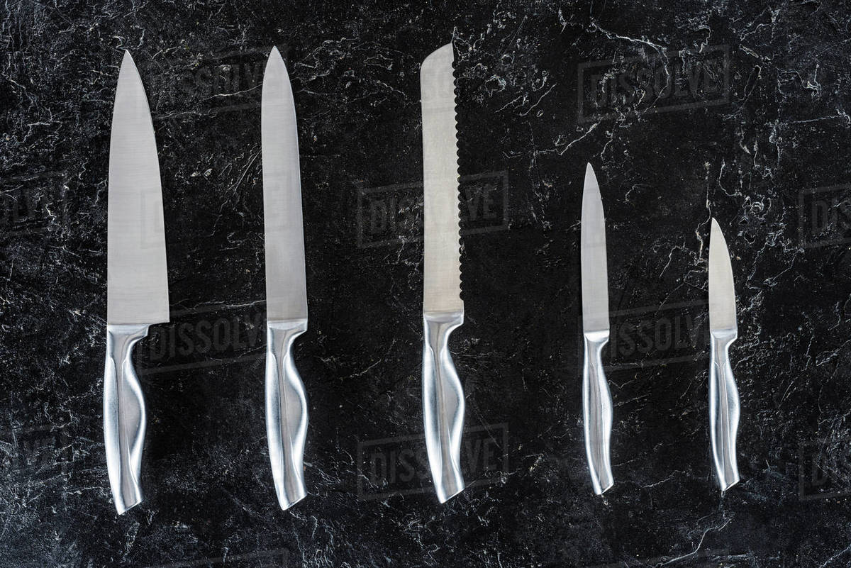 Top view of different kitchen knives arranged on black surface ...