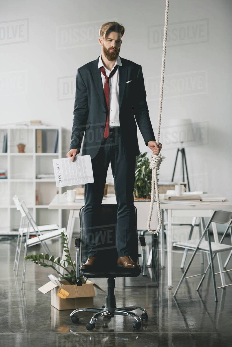 Depressed young fired businessman standing on chair and trying to hang ...