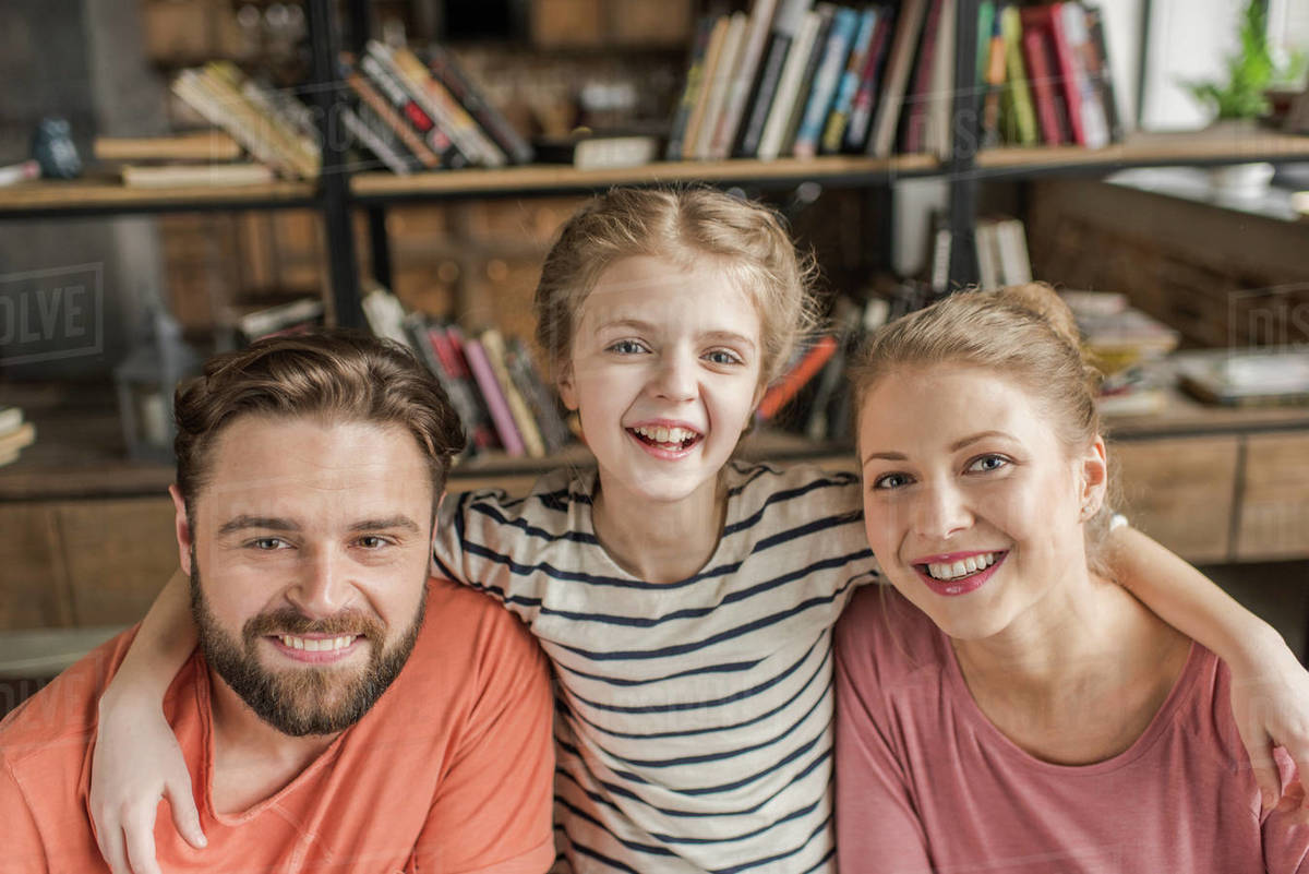 Happy young family with one child embracing and smiling at camera ...