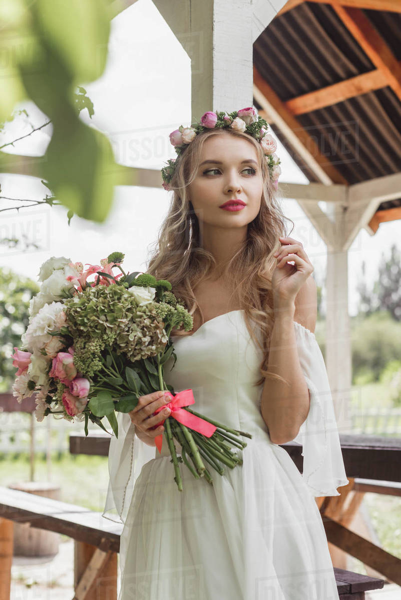 beautiful thoughtful young bride holding bouquet of flowers and looking ...