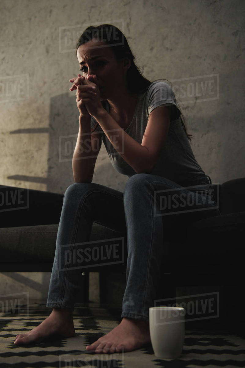 bottom view of crying woman sitting on sofa with coffee cup on floor ...