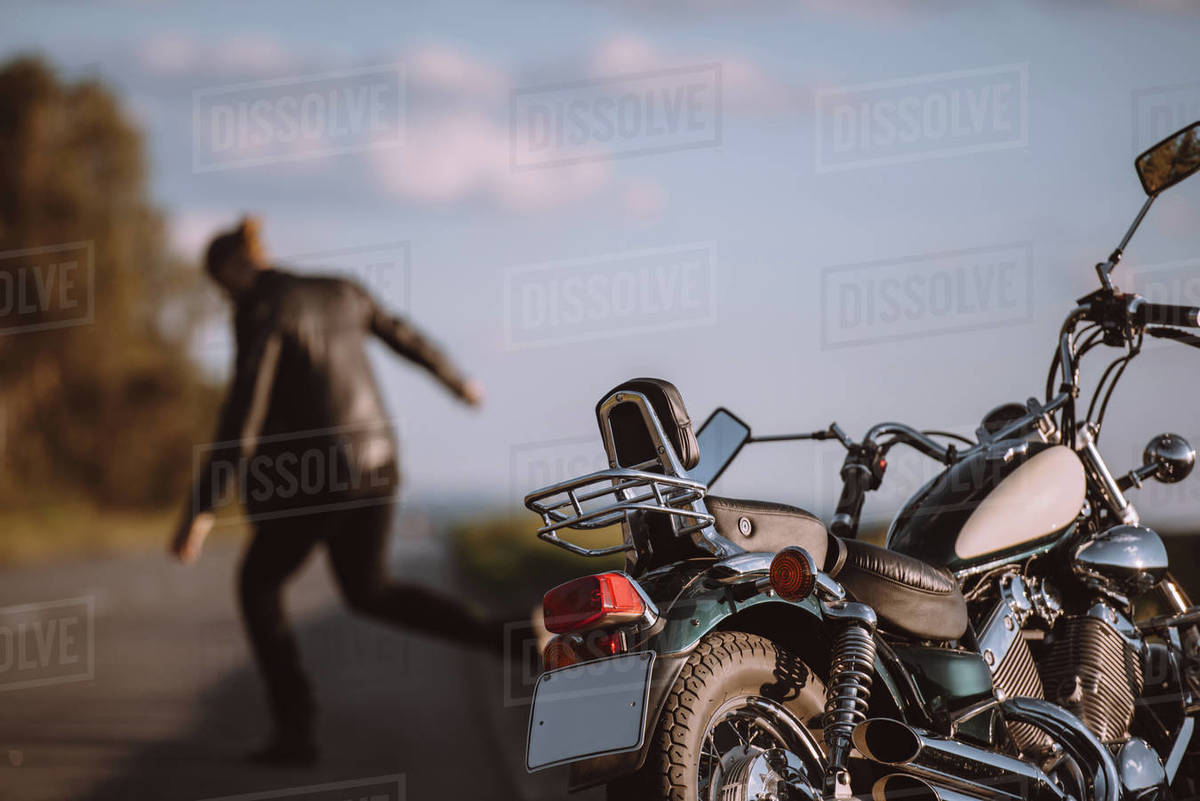 Broken classical motorcycle on road with angry biker on background ...