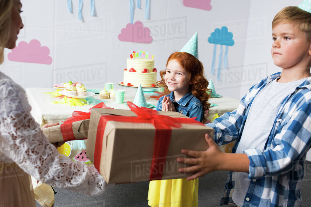 side view of kids presenting gifts to cute happy girl at birthday party ...