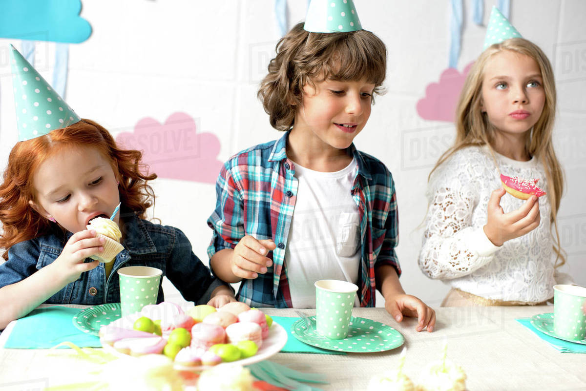 adorable little kids in party hats eating delicious sweets at birthday ...
