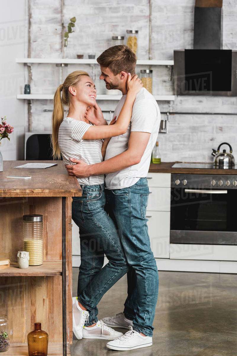 side view of couple hugging in kitchen and leaning on kitchen counter ...