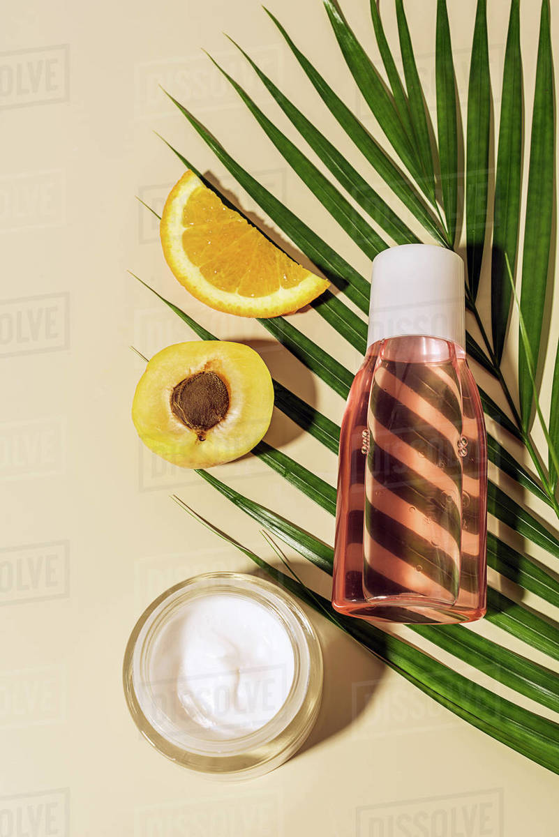 top view of body cream and lotion, fruits and green palm leaf on beige ...