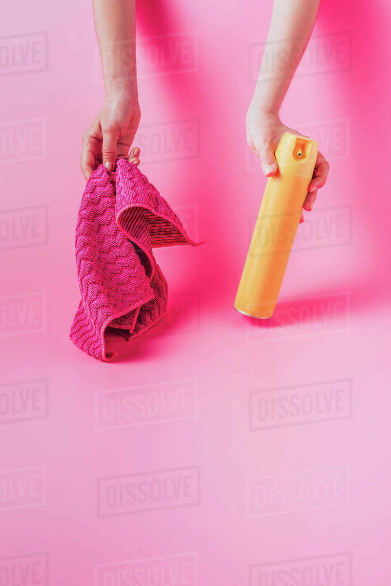 cropped image of woman holding spray can and rag, pink background ...