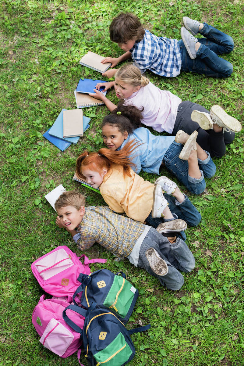 top view of cute little kids reading books while lying on grass and ...