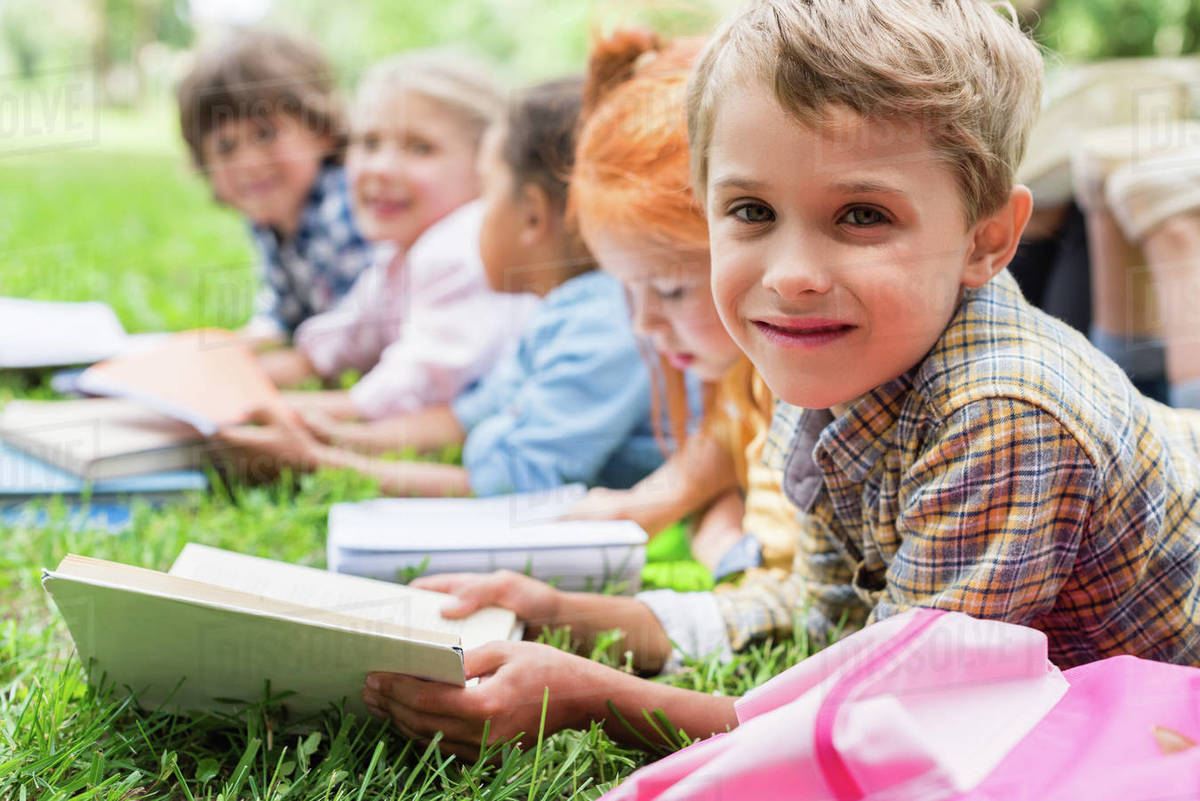 adorable little kids reading books while lying on grass in park ...