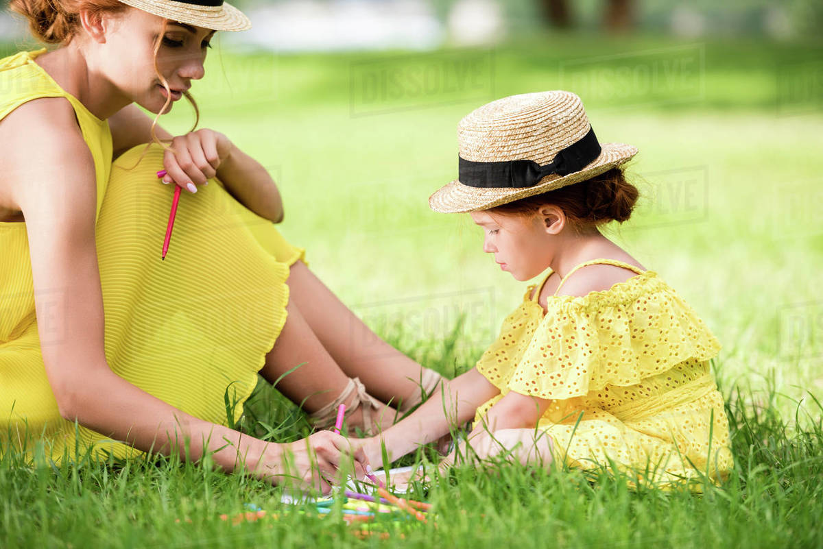 Side view of beautiful mother and daughter drawing together while ...