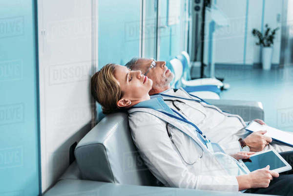 Side view of tired male and female doctors sleeping with clipboard and ...