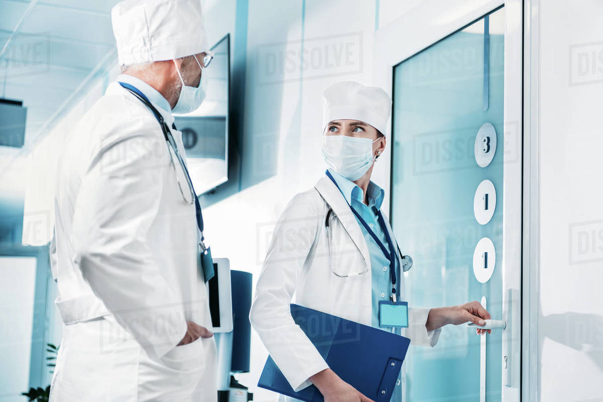 Female doctor with clipboard opening door and talking to male colleague ...