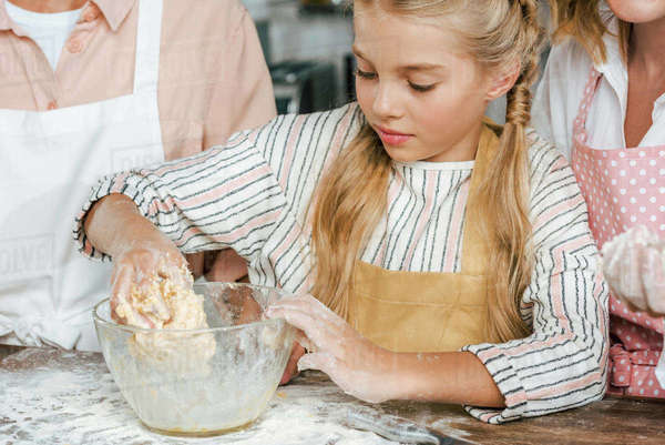 Cropped shot of concentrated little child making dough with parents at ...
