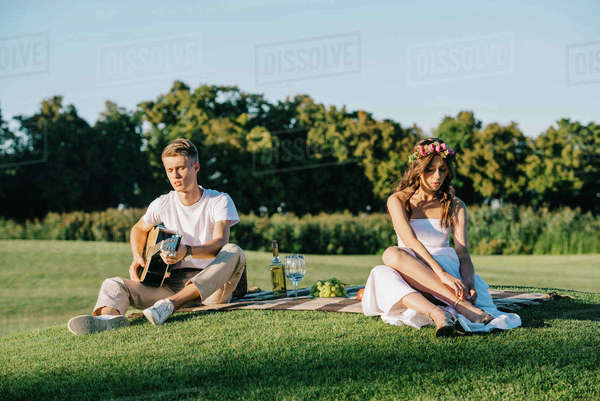 Groom playing guitar for upset bride during romantic picnic on lawn ...