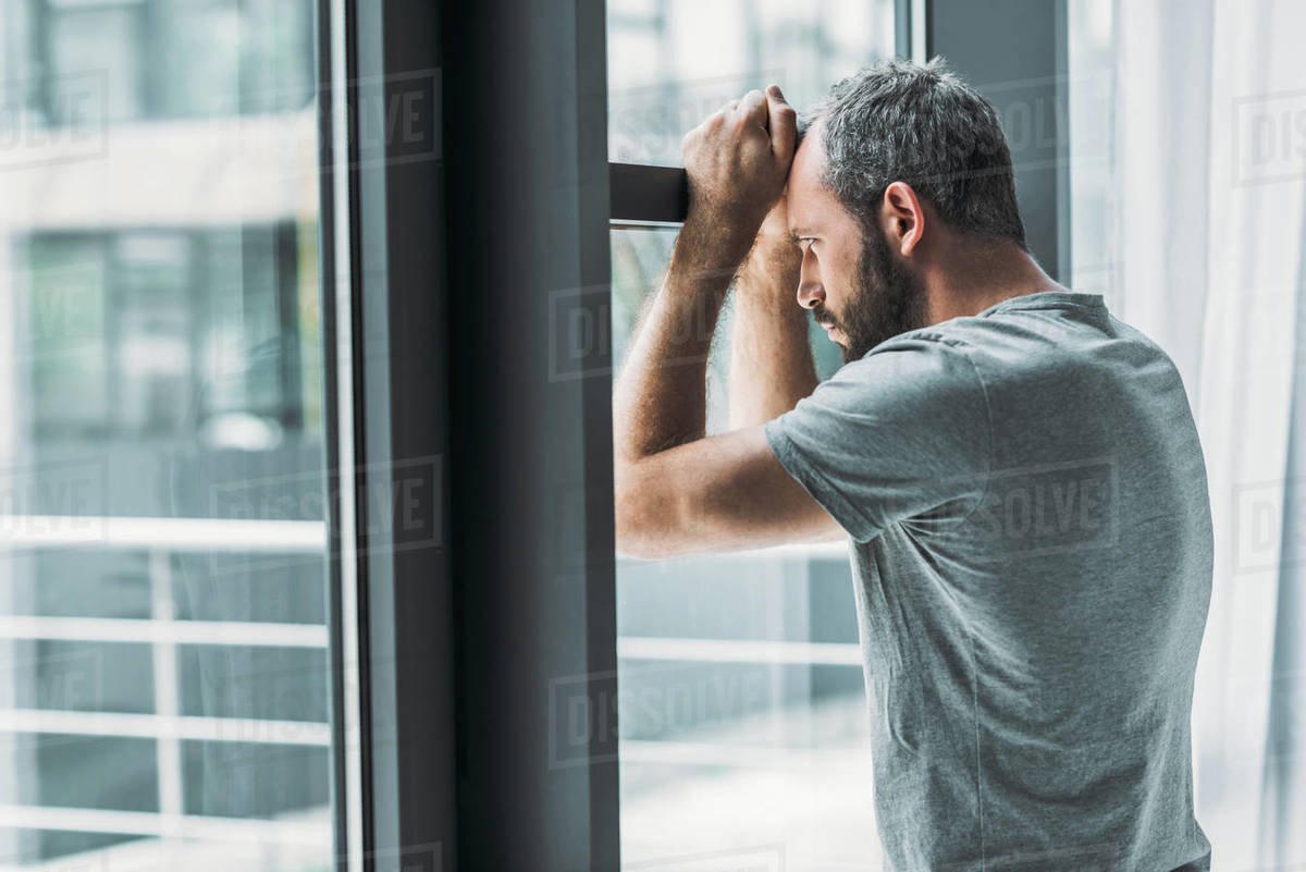Depressed bearded man leaning at window and looking through it - Stock ...