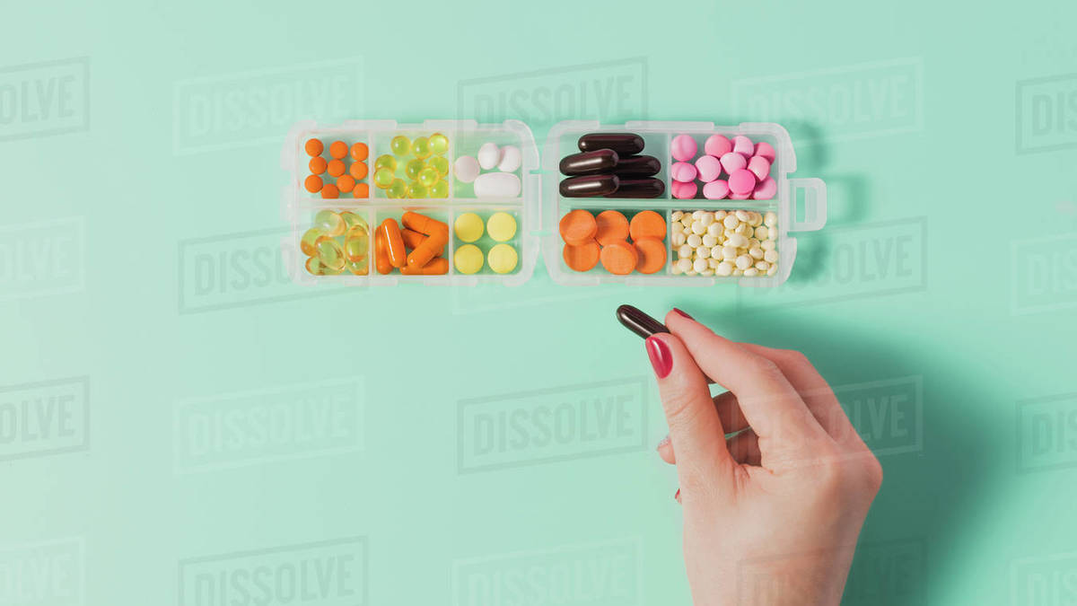 Cropped shot of woman taking capsule from plastic case with various ...