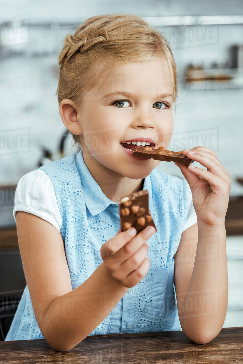 Cute happy kid eating delicious chocolate with hazelnuts and smiling at ...