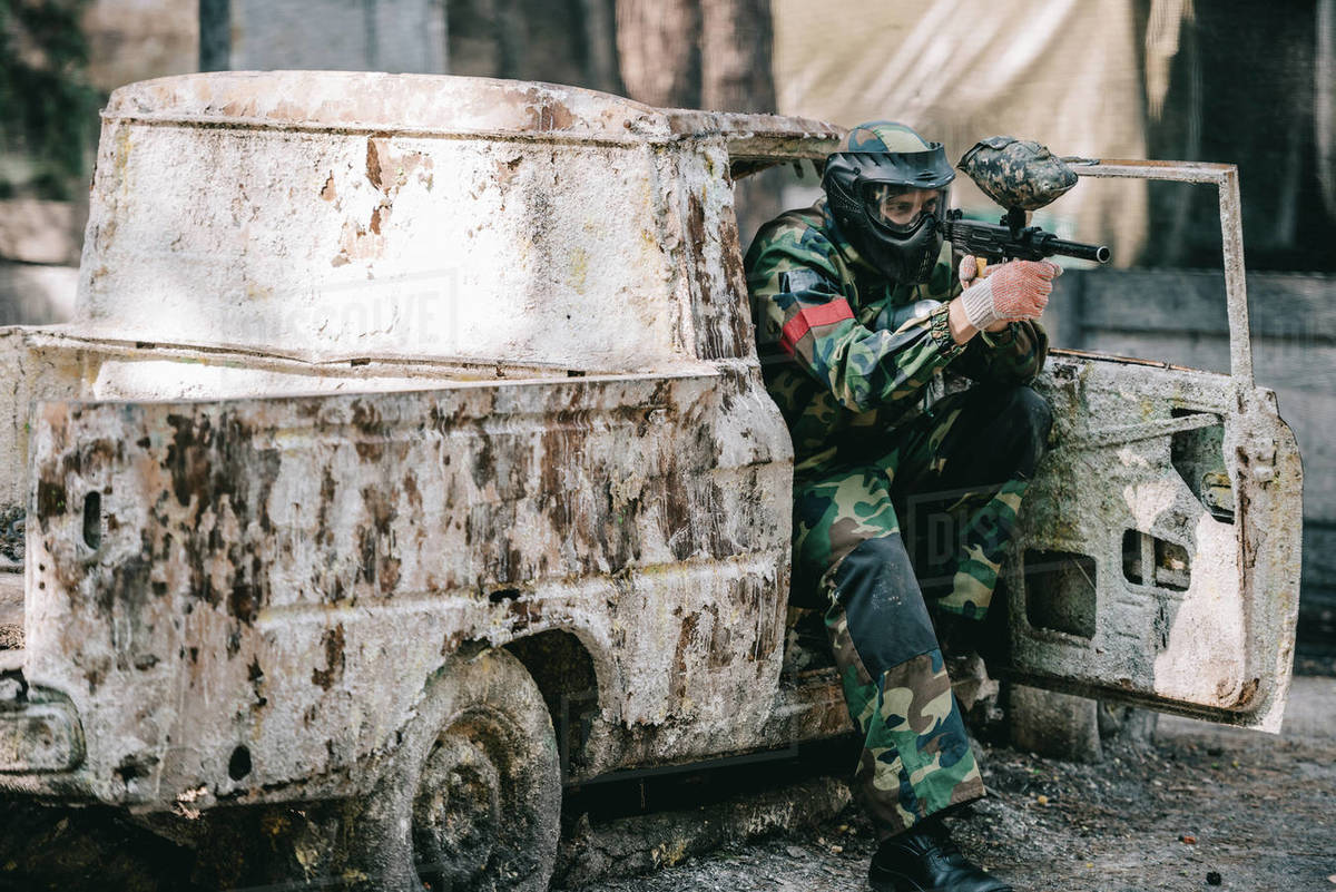 Male paintball player in goggle mask and camouflage aiming by paintball ...