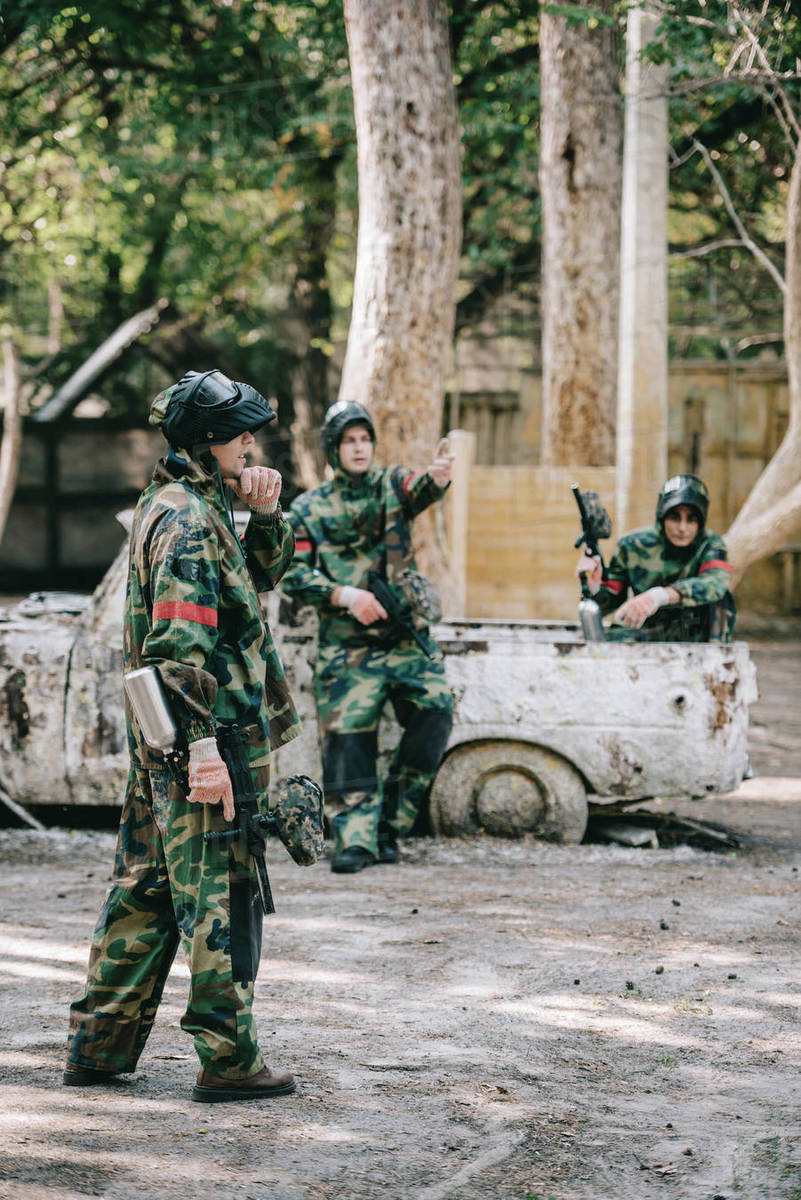 Male paintballer in camouflage pointing by hand to his team near broken ...